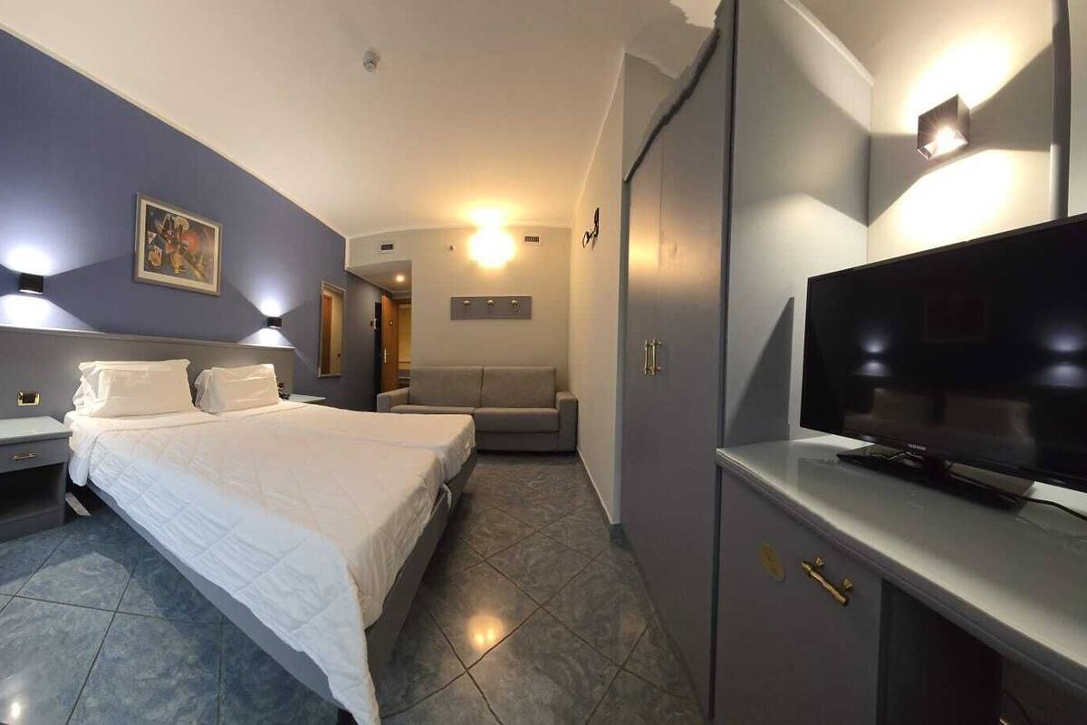 Quarto de hotel com cama, televisão, escrivaninha e sofá.