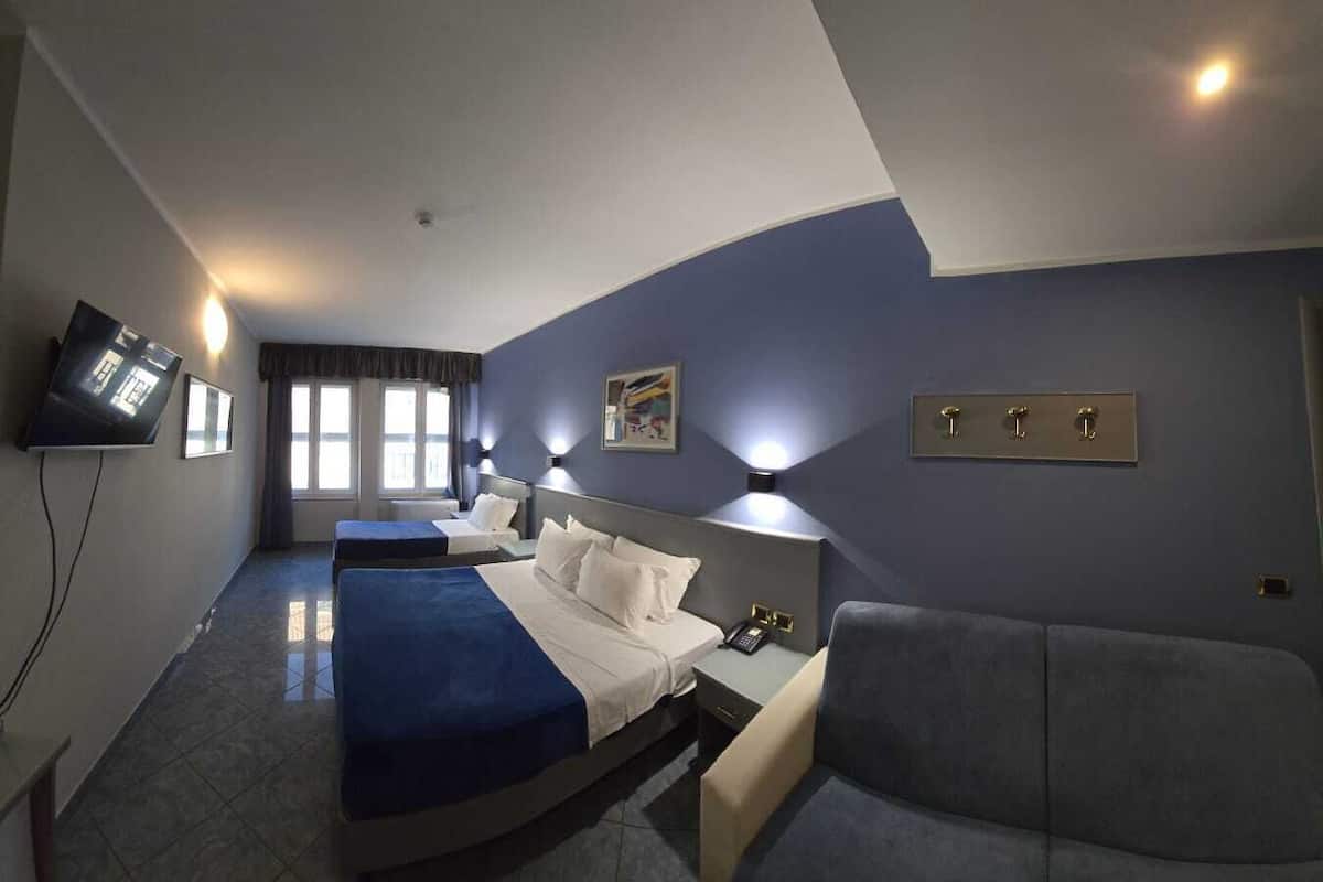 Quarto de hotel com duas camas, uma escrivaninha, uma cadeira, uma televisão e uma janela com cortinas.