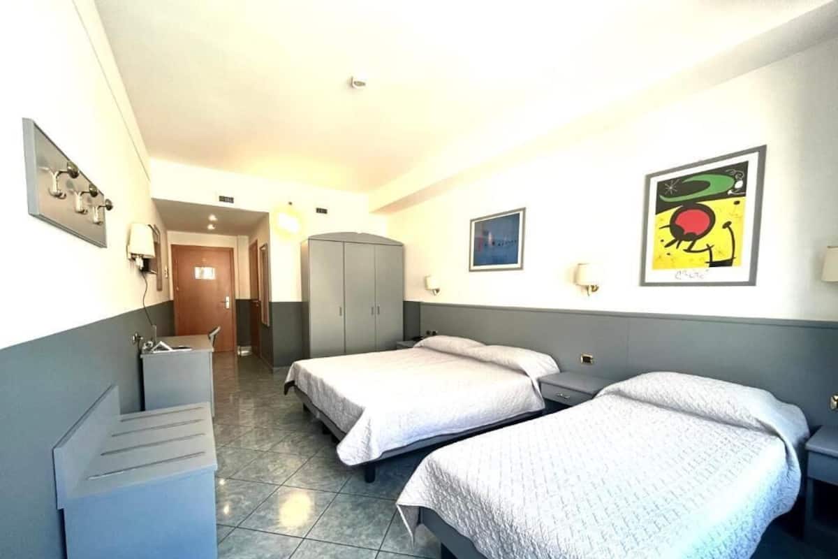 Quarto de hotel com duas camas, um guarda-roupa, uma escrivaninha e uma casa de banho.