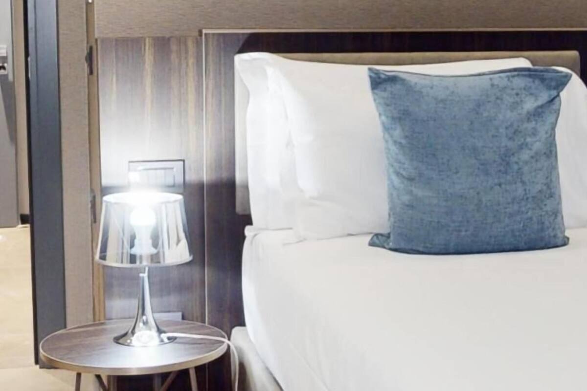 Quarto de hotel com cama, mesa de cabeceira e abajur.