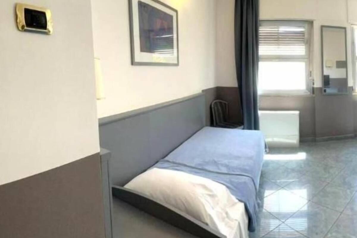 Quarto de hotel com cama, mesa pequena, cadeira, espelho e janela com cortinas.