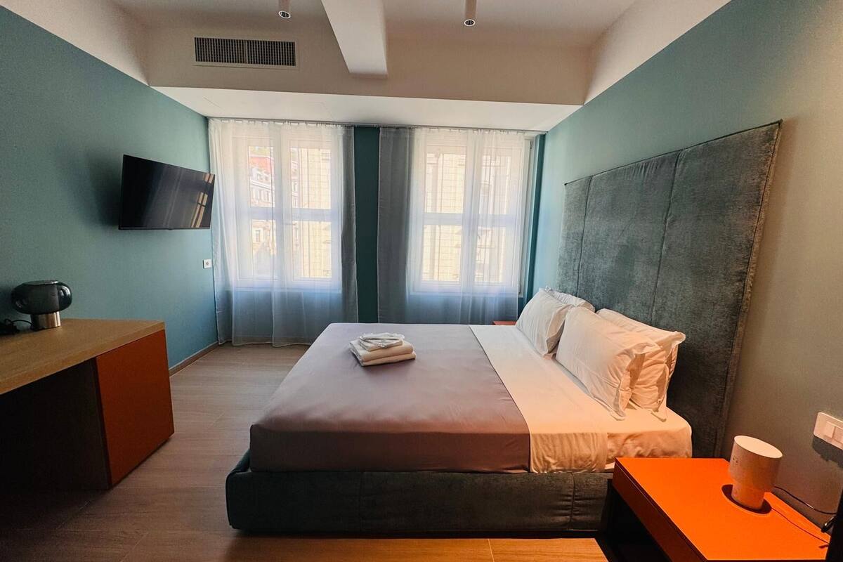 Quarto de hotel moderno com cama, televisão, escrivaninha e janela com cortinas.