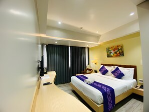 Quarto de hotel com cama, mesas de cabeceira, escrivaninha e um quadro na parede.