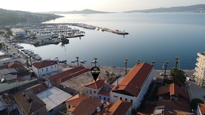 Uma marina costeira com barcos atracados, um cais que se estende sobre a água e edifícios com telhados de terracota.