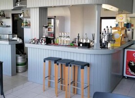 Uma área de bar com banquetas, geladeira e prateleiras com garrafas.