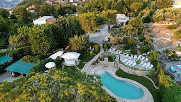 Vista aérea de um resort com piscina, espreguiçadeiras e montanhas ao fundo.