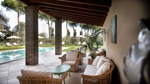 Uma área de estar coberta ao ar livre com móveis de vime, piscina e vista para o jardim.