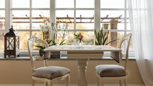 Uma sala de jantar com uma mesa e duas cadeiras, um vaso com flores e vista pela janela.
