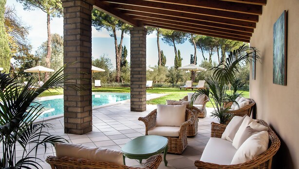 Uma área de varanda coberta com móveis de vime, piscina e vista para a paisagem ao redor.