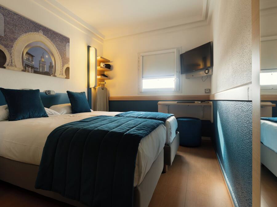 Quarto de hotel com uma cama grande, uma escrivaninha, uma televisão e uma janela.