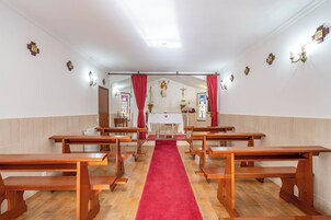 Interior de igreja com bancos de madeira, um tapete vermelho que leva ao altar e estátuas religiosas nas paredes.