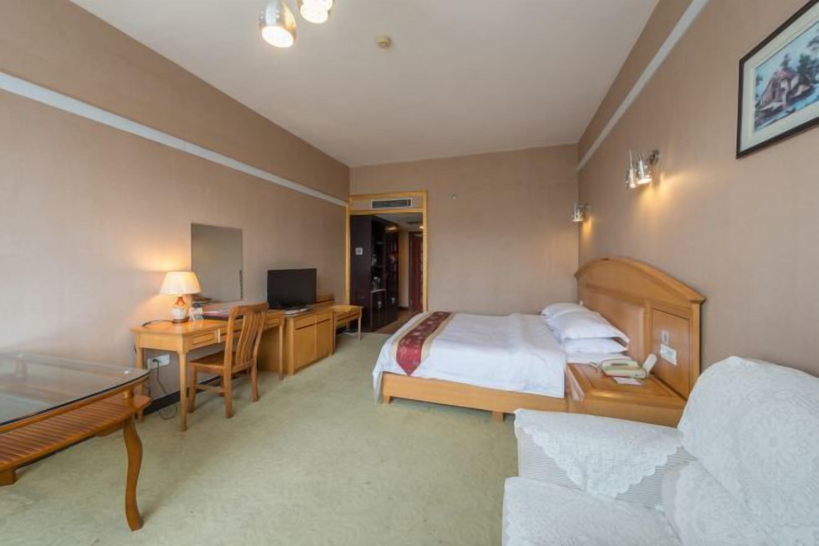 Quarto de hotel com uma cama, uma escrivaninha, uma cadeira, uma televisão e um abajur.