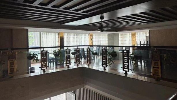 Um espaço amplo com teto alto, varanda com guarda-corpo de vidro e vista para o exterior.