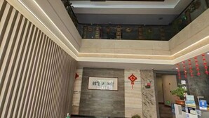 Um hall de hotel com design moderno, com teto alto, balcão de recepção e uma parede decorativa com uma placa.