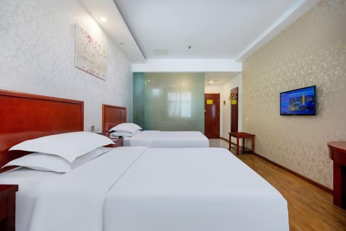 Quarto de hotel com duas camas, televisão e piso de madeira.