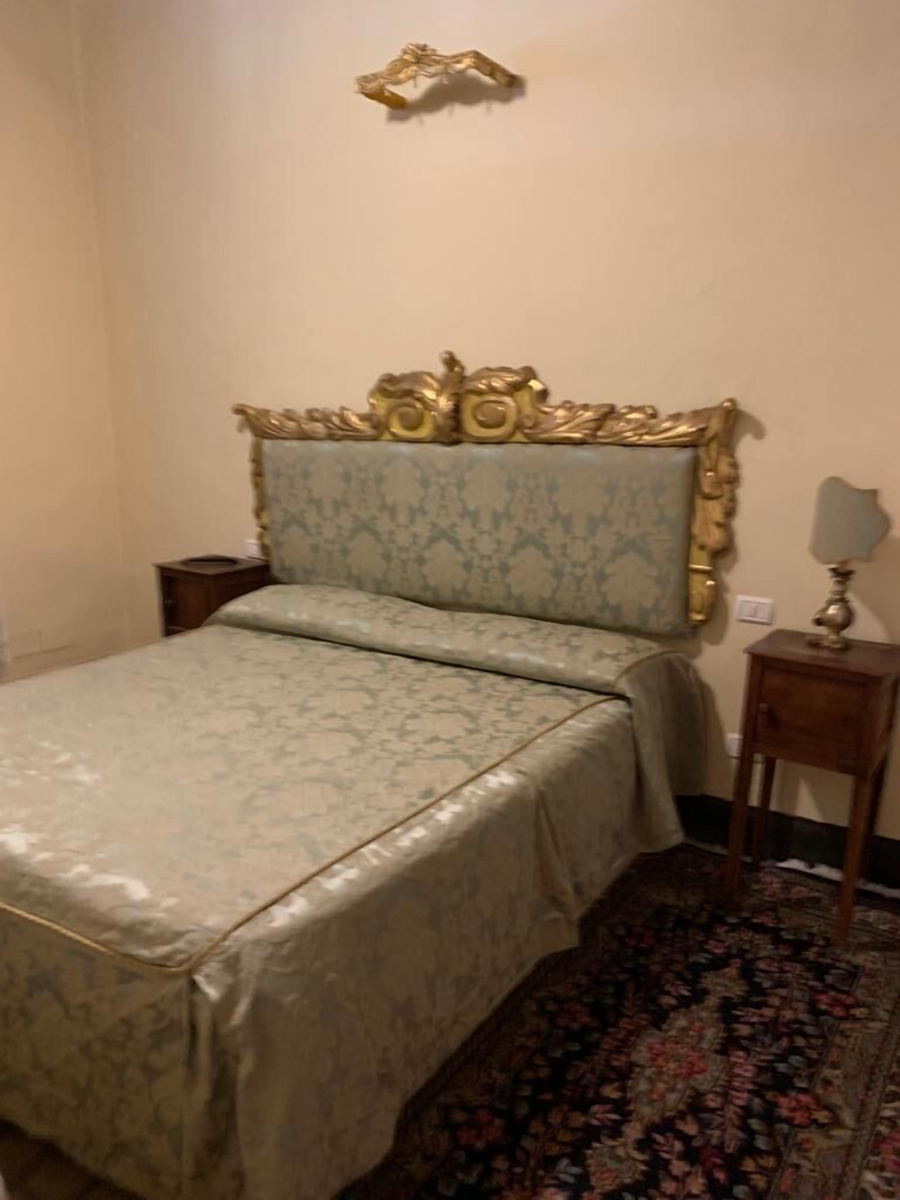 Quarto com cama, mesa de cabeceira, luminária e tapete estampado.