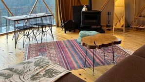 Interior acolhedor de uma cúpula geodésica, com piso de madeira, mesa de jantar com cadeiras, lareira e uma grande janela com vista para as montanhas.
