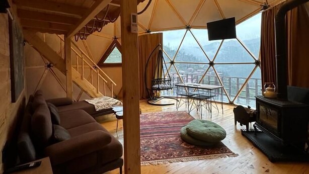 Um interior aconchegante com escada de madeira, um sofá, área de refeições e lareira.