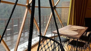 Um ambiente acolhedor com uma cadeira suspensa, uma mesa com jogos americanos e vista através de grandes janelas.