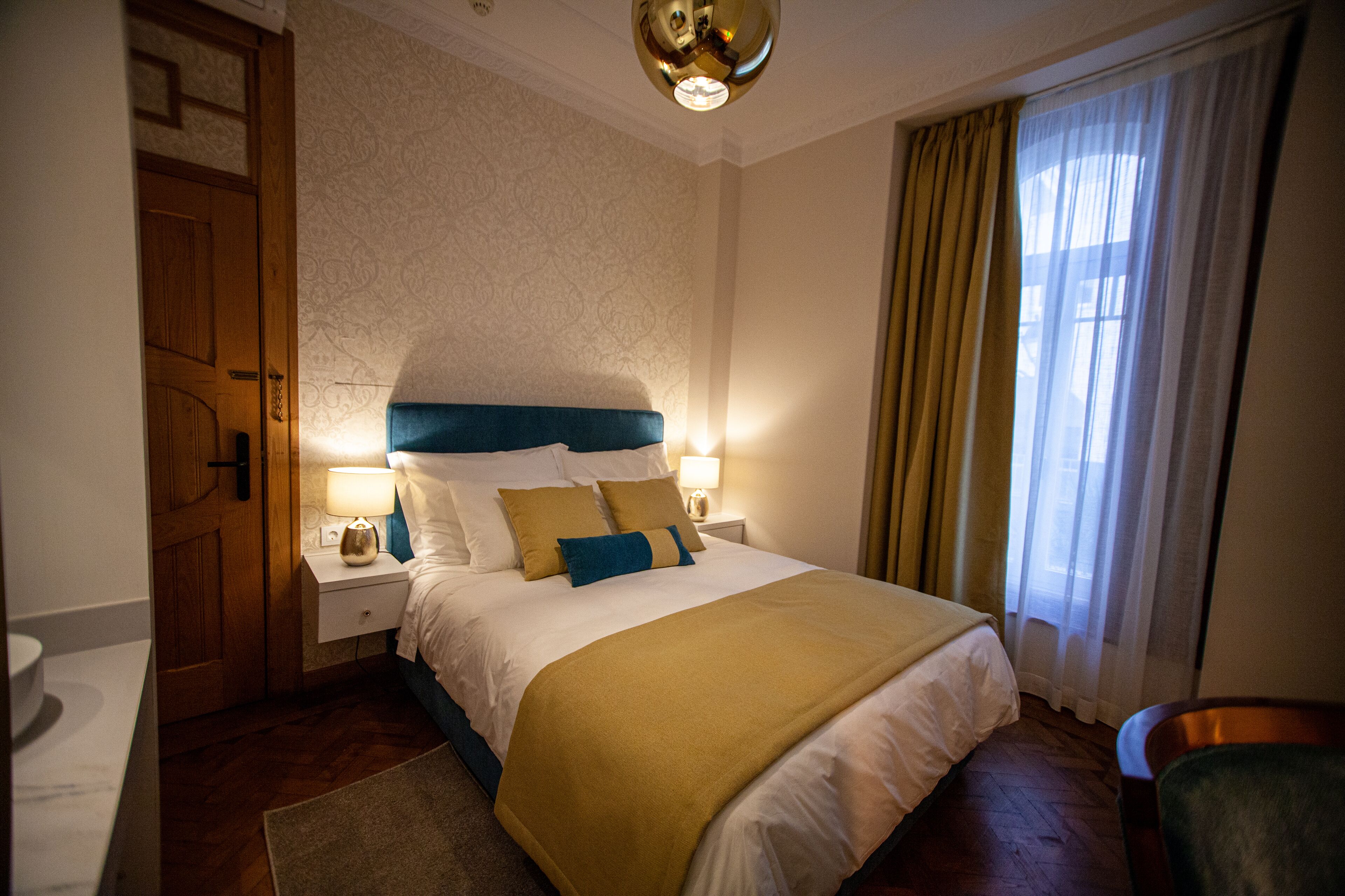 Quarto bem arrumado com cama, mesas de cabeceira e janela com cortinas.
