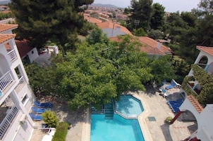 Piscina rodeada por árvores e edifícios brancos com telhados de telhas vermelhas.
