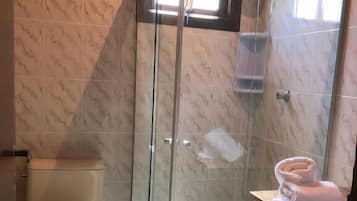 Um banheiro com chuveiro em box de vidro, vaso sanitário e porta-toalhas.