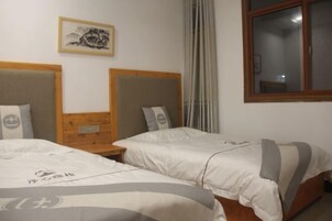 Quarto de hotel com duas camas, cabeceira de madeira, mesa de cabeceira, quadro emoldurado na parede e janela com cortinas.