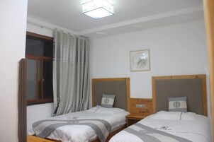 Quarto com duas camas, janela com cortinas, quadro na parede e luminária no teto.