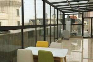 Varanda com toldo de vidro, mesa e cadeiras.