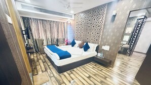 Quarto de hotel moderno com uma cama grande, piso de madeira, um painel decorativo na parede e uma área de estar com uma cadeira e uma mesa pequena.