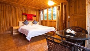 Quarto de madeira com cama, uma mesa e uma tigela de frutas, além de uma janela.