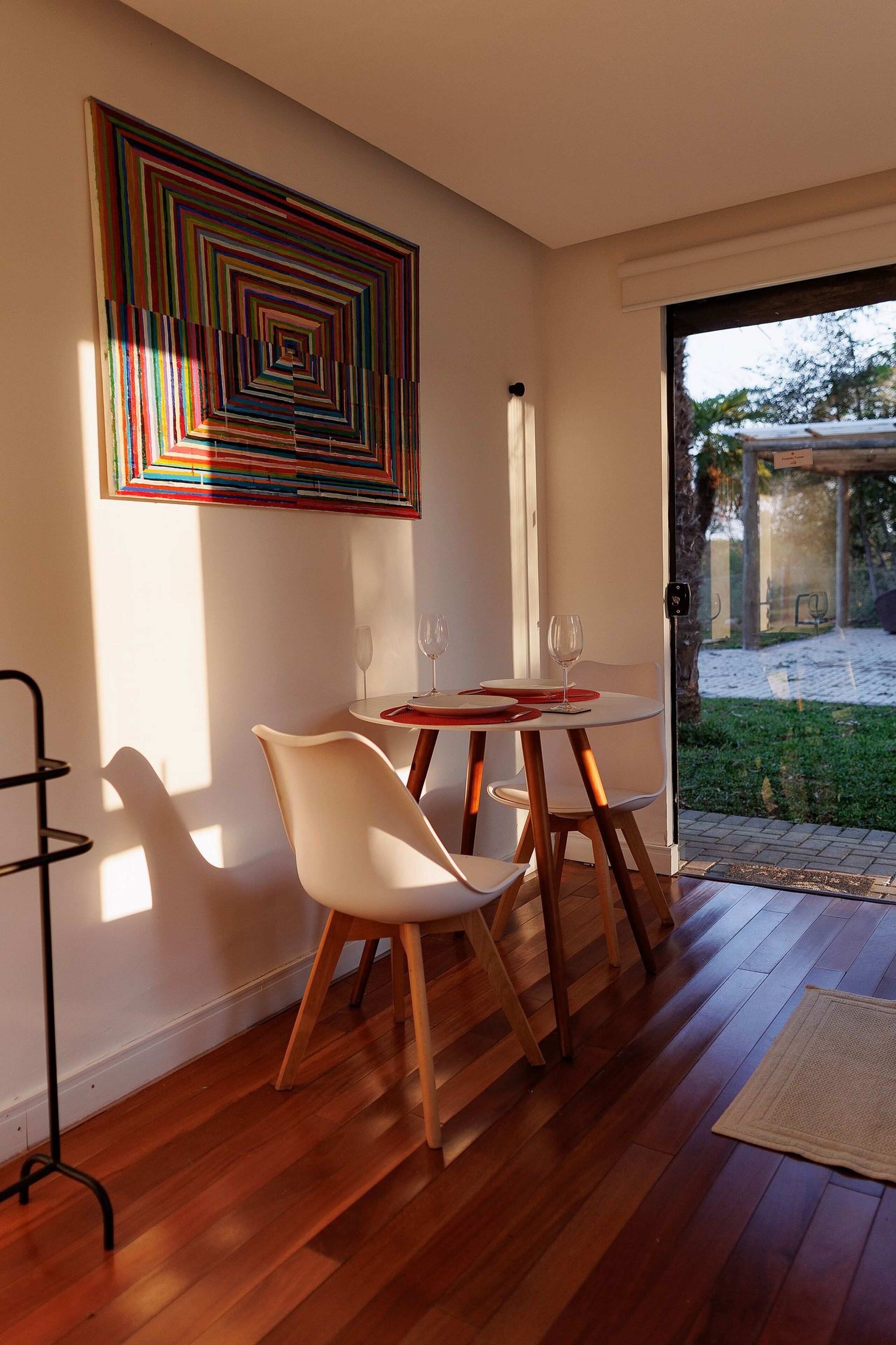 Uma área de refeições com mesa, cadeiras e uma pintura abstrata e colorida na parede.