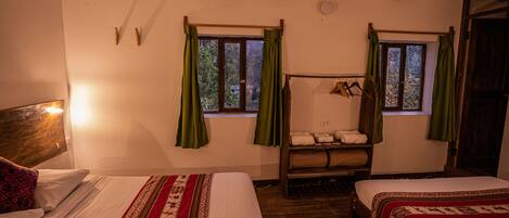 Quarto com duas camas, vigas de madeira no teto, uma janela com cortinas e uma estante com toalhas.