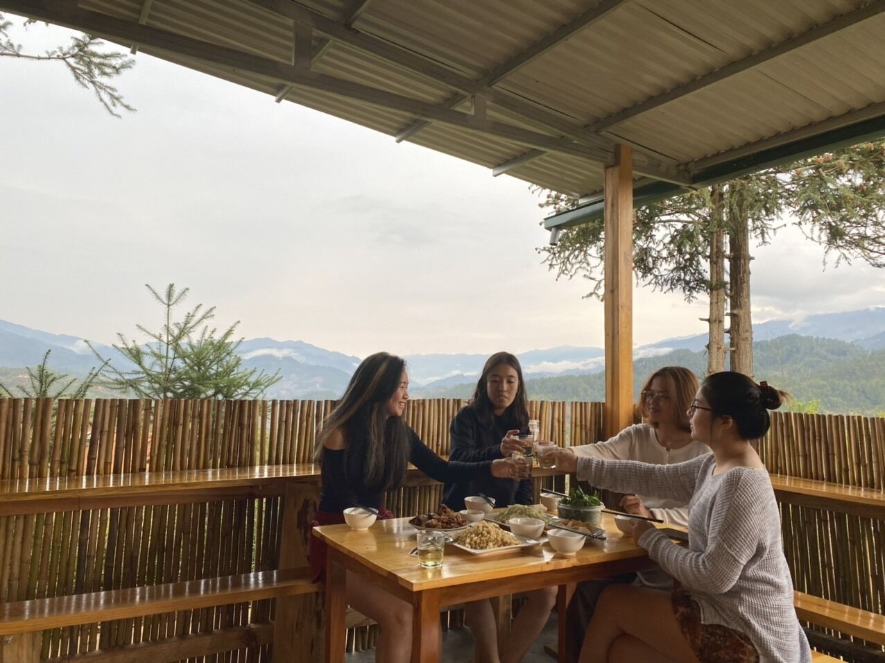 Um grupo de pessoas sentadas em uma mesa de madeira, com vista para montanhas ao fundo.