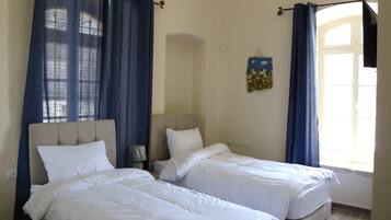 Quarto de hotel com duas camas de solteiro, janela com cortinas, uma obra de arte na parede e uma pequena mesa de cabeceira com abajur.