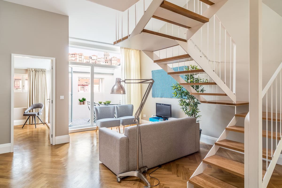 Uma sala de estar moderna com escada, um sofá, uma poltrona, uma luminária e uma televisão.
