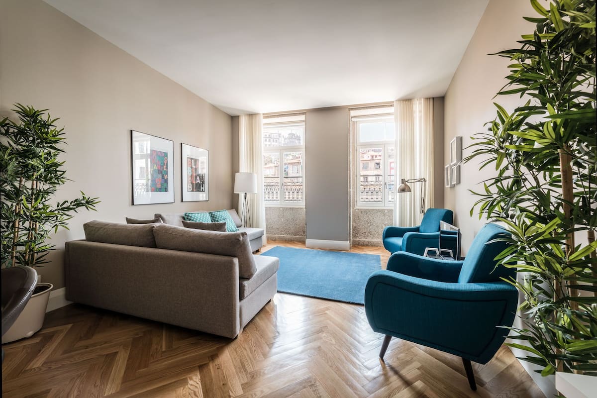 Uma sala de estar moderna com sofá, poltronas e uma grande janela com vista para edifícios.