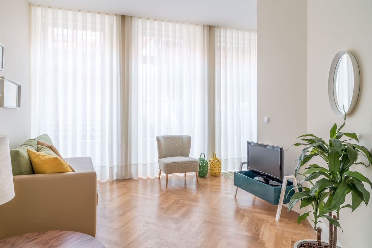 Sala de estar com sofá, poltrona, televisão e planta em vaso.