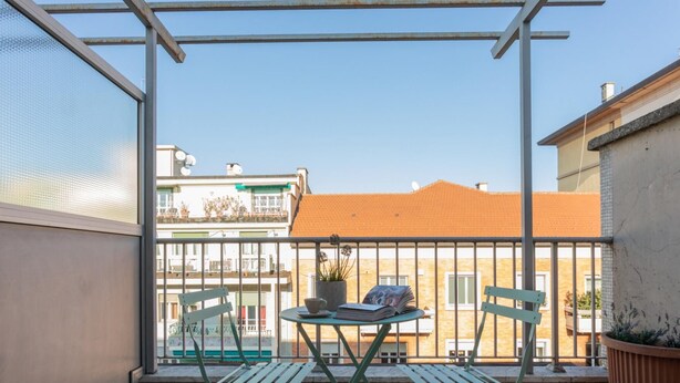 Varanda com mesa, cadeiras, um vaso de planta e vista para edifícios.