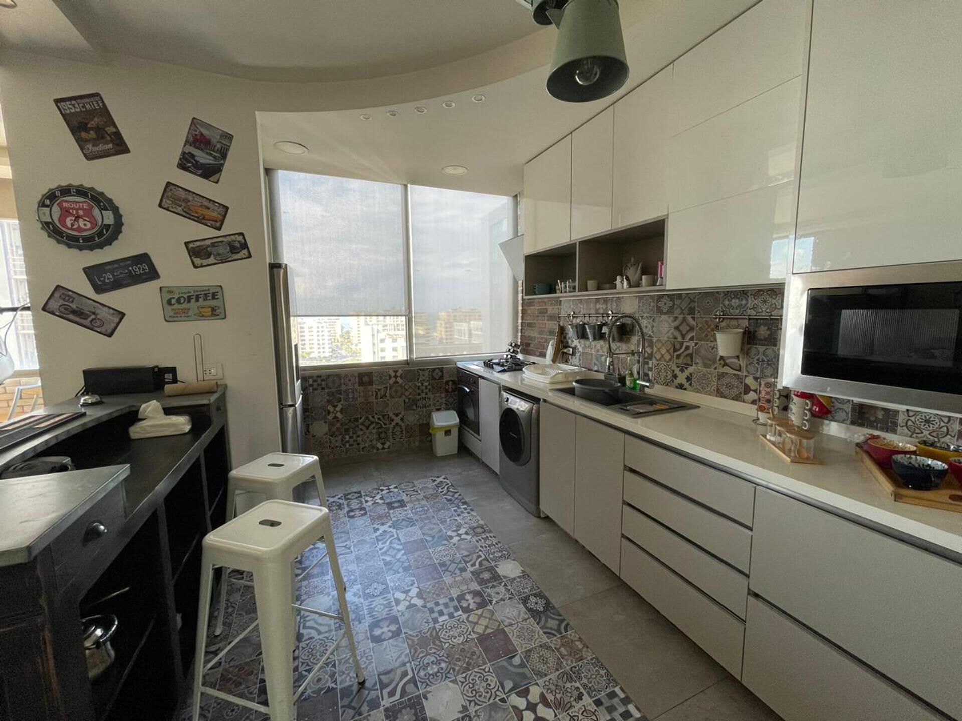 Uma cozinha moderna com armários brancos, painel de azulejos, uma janela grande e um micro-ondas.