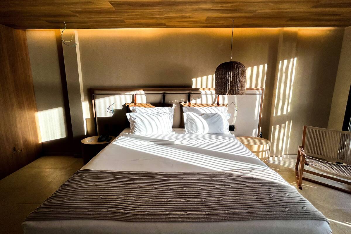 Quarto de hotel com uma cama grande, mesa de cabeceira com abajur e uma cadeira.