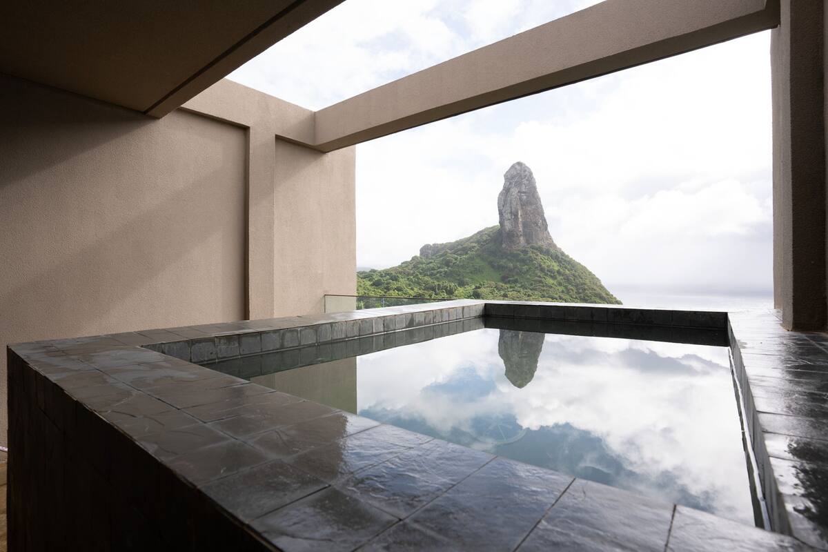 Uma piscina infinita moderna com vista clara para o topo de uma montanha através de uma grande janela.