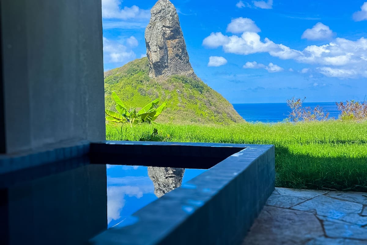 Vista de uma formação rochosa natural pela janela, com um céu azul límpido e uma área gramada ao primeiro plano.