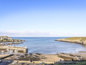 Uma vila costeira com um porto, litoral rochoso e vista clara do mar.