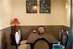 Uma área de refeições com parede de tijolos, uma mesa com cadeiras, um abajur vermelho e duas obras de arte emolduradas na parede.