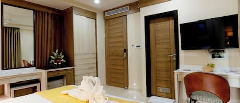 Quarto de hotel com cama, escrivaninha, cadeira, televisão e guarda-roupa.