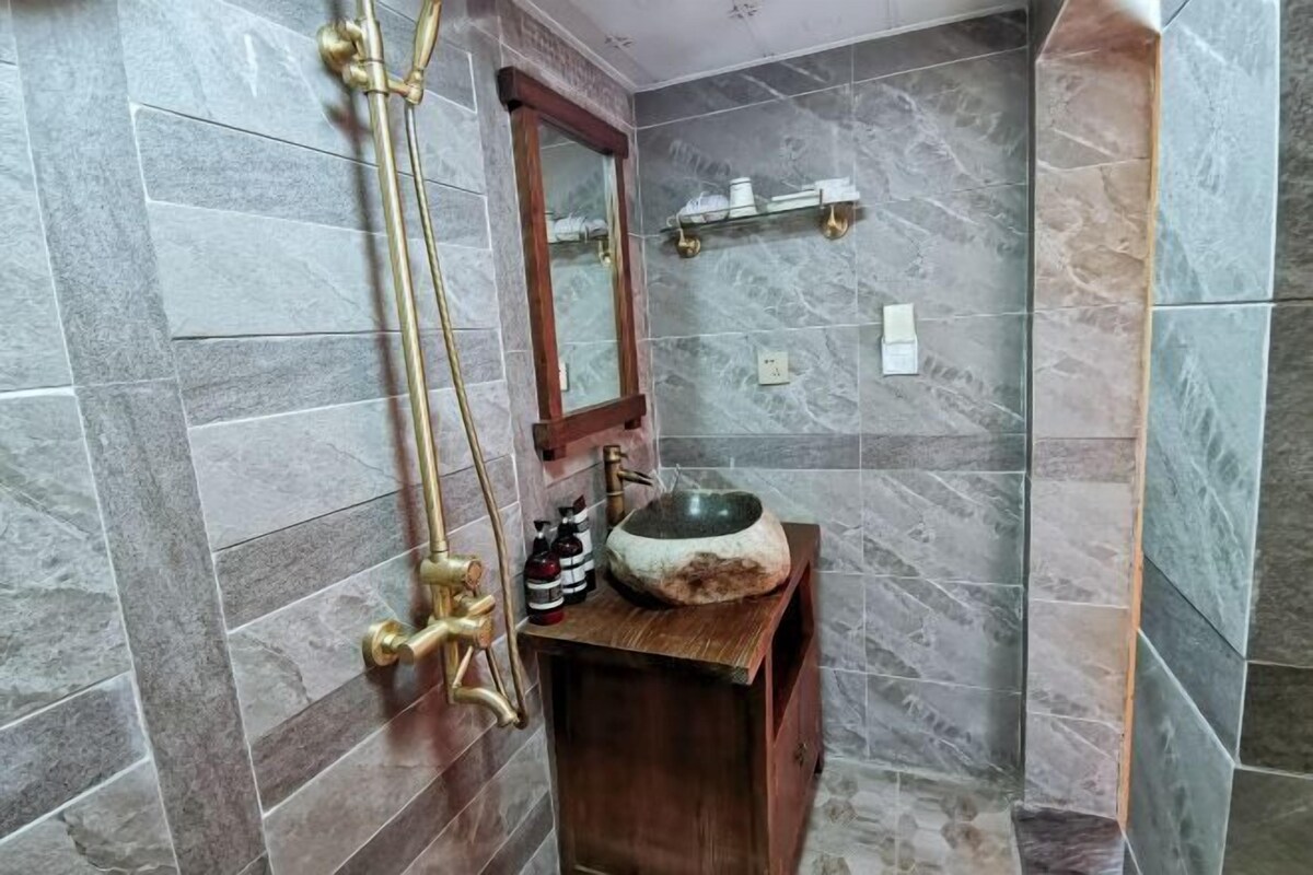 Um banheiro com parede de azulejos de pedra, um móvel de vaidade de madeira com cuba, um espelho e um porta-toalhas.