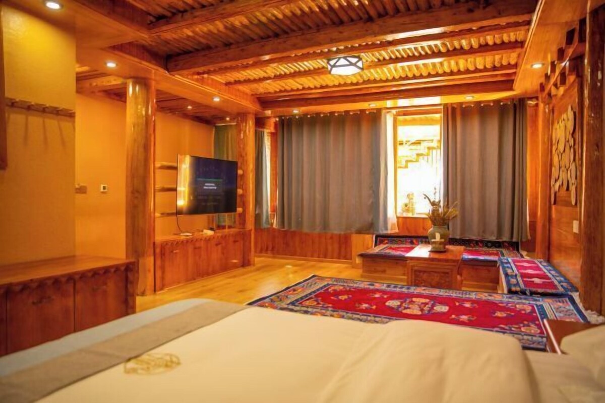 Quarto de hotel com teto de madeira, uma cama, televisão e uma janela grande com cortinas.