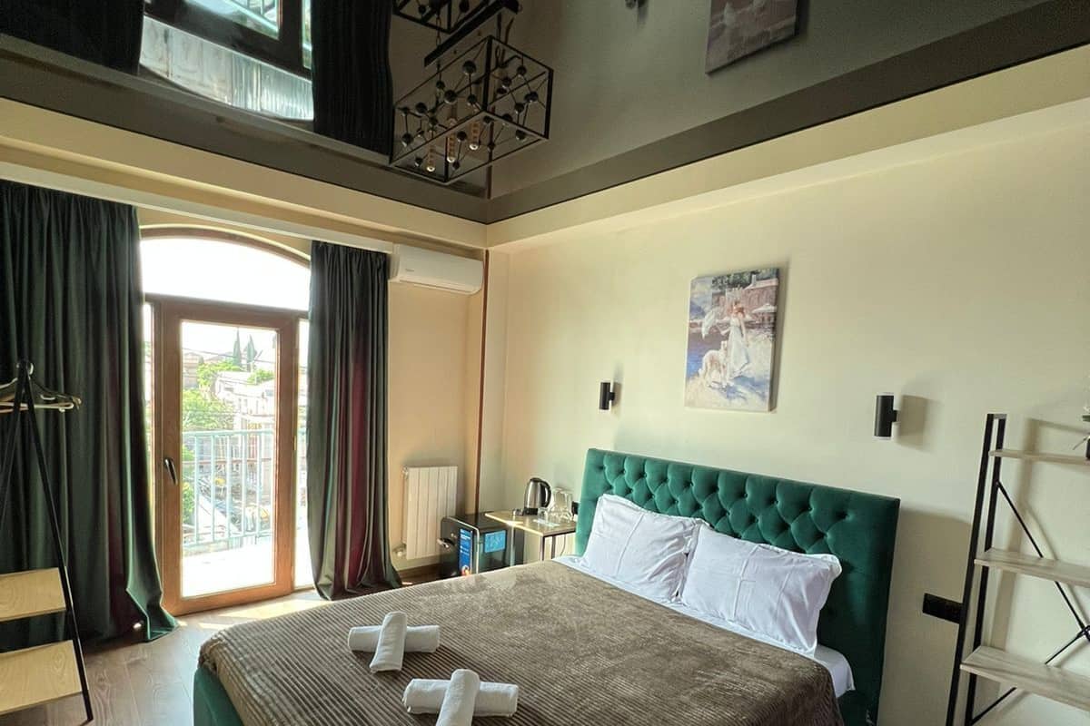 Quarto de hotel com uma cama grande, uma escrivaninha com cadeira, uma janela com cortinas e vista para o exterior.