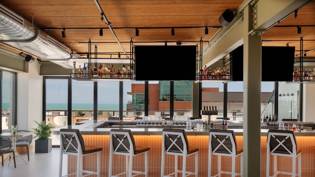 Uma área de bar moderna com balcão alto, vários bancos e vista para o oceano.